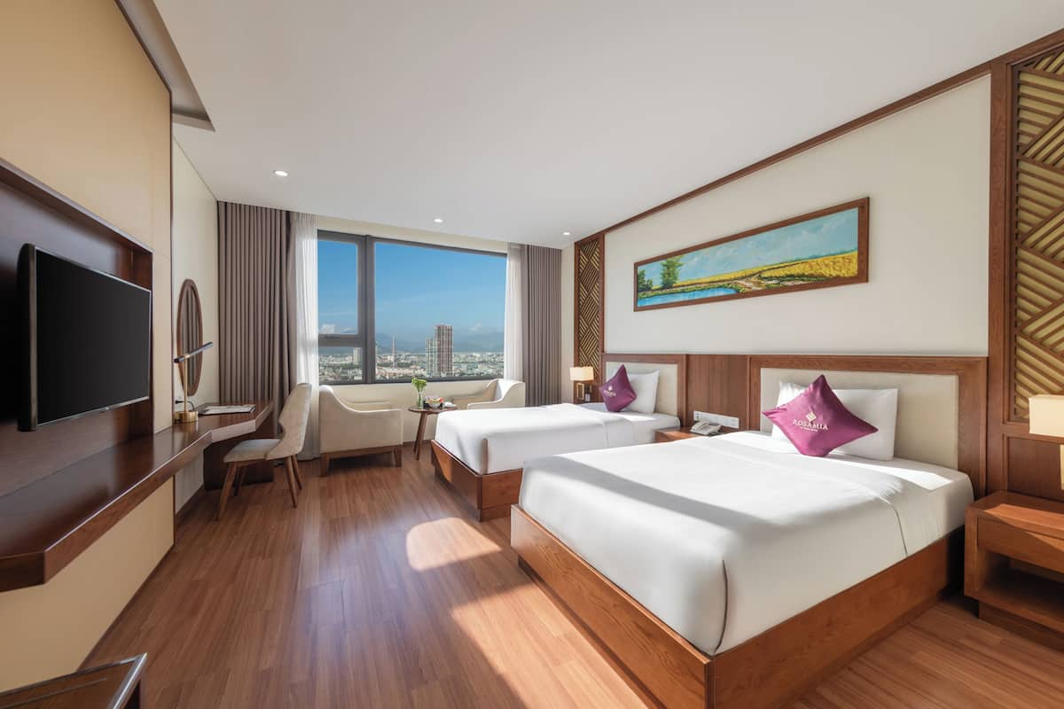 Quarto de hotel com duas camas, televisão, escrivaninha e vista da cidade.