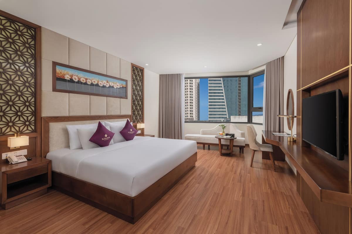 Quarto de hotel com uma cama grande, escrivaninha, televisão e vista para a cidade.