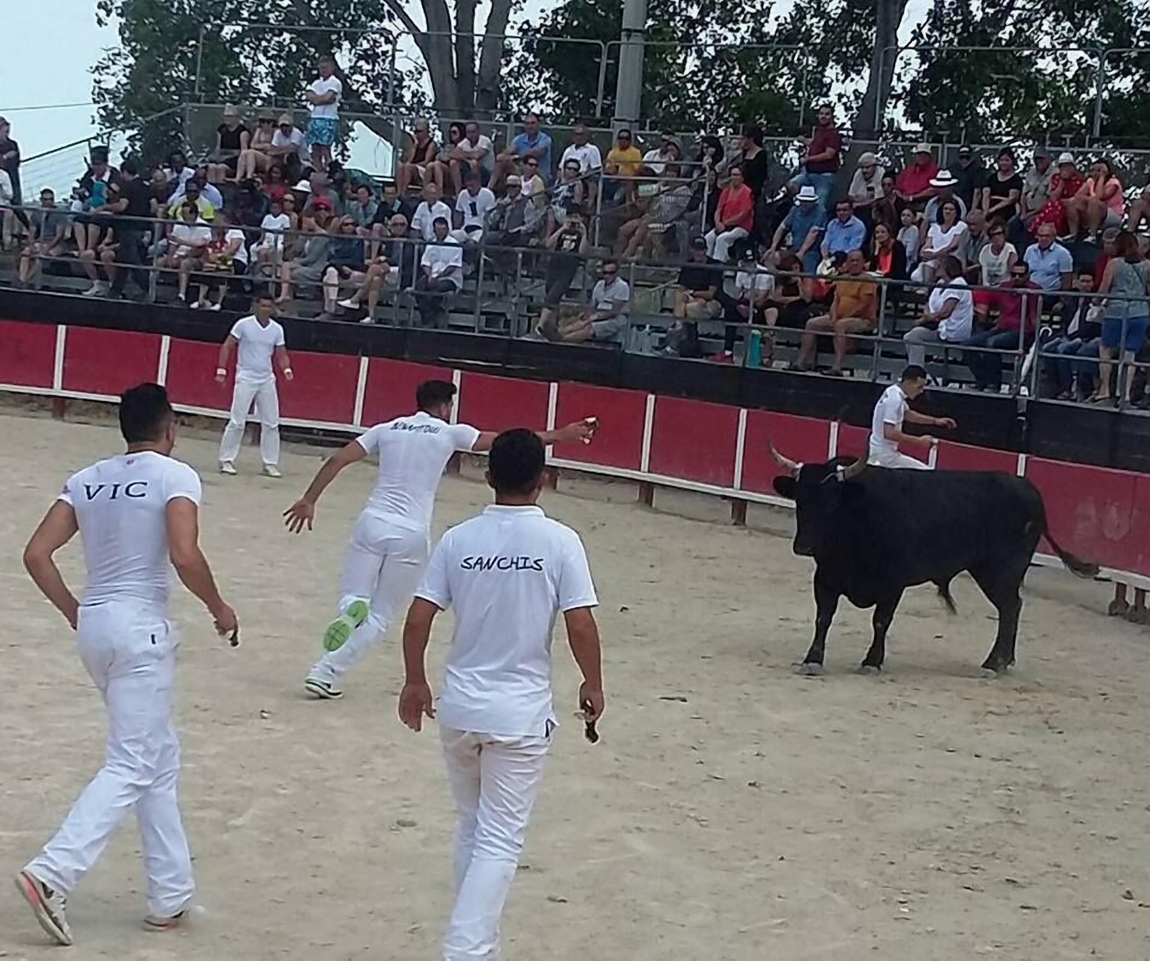 Uma arena de touradas com espectadores nas arquibancadas e toureiros trajados de branco.