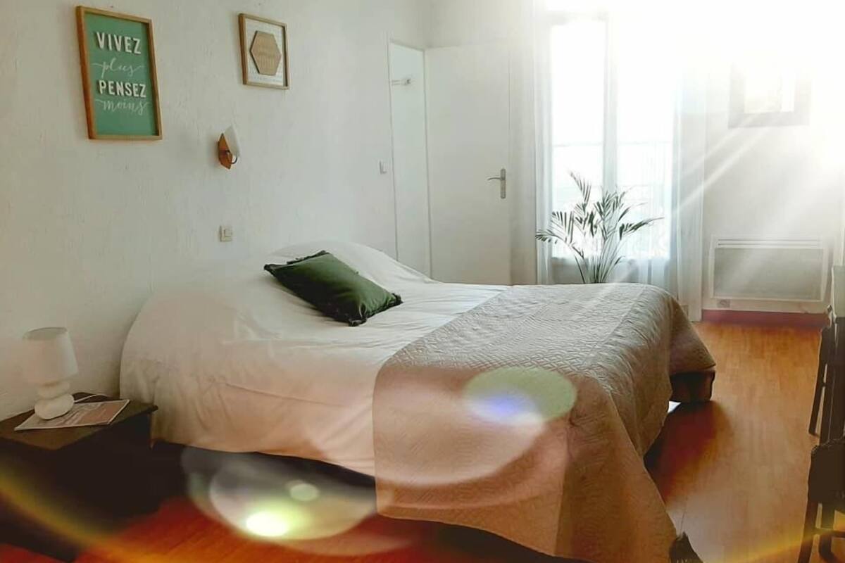 Quarto com cama, mesa de cabeceira, uma frase emoldurada na parede e uma porta.