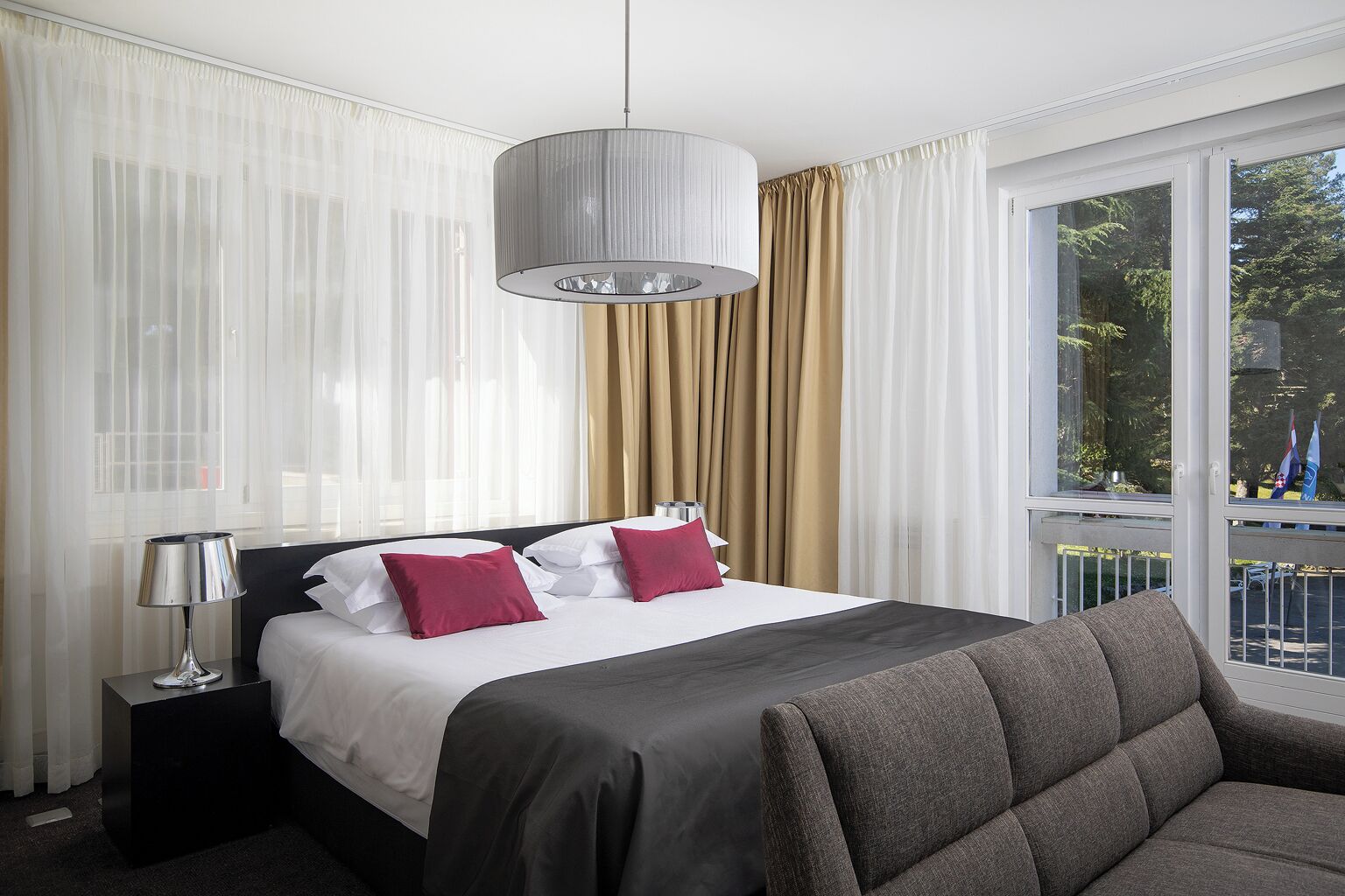 Quarto de hotel com cama, mesa de cabeceira, luminária e vista para o exterior.