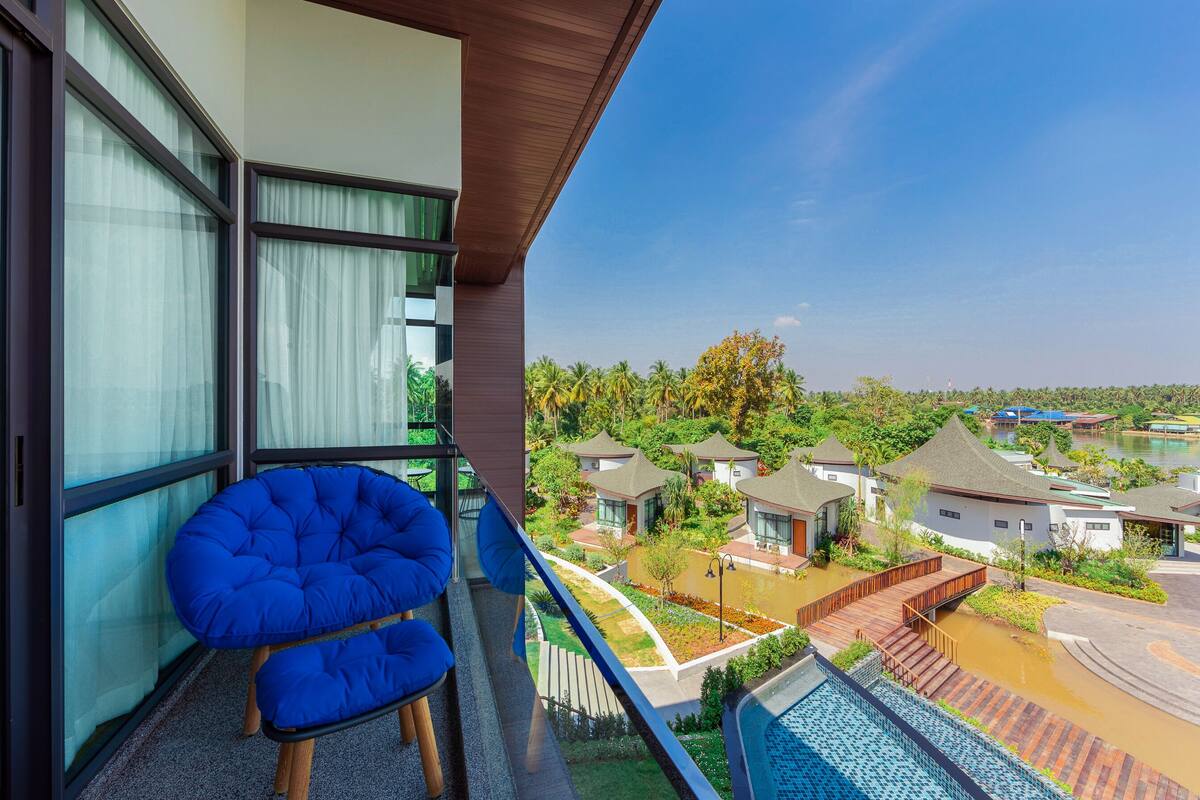 Uma varanda com uma cadeira azul estofada, vista para uma área residencial com casas e uma piscina.