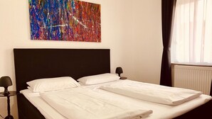 Cama bem arrumada com lençóis brancos, cabeceira preta e uma pintura abstrata colorida acima.
