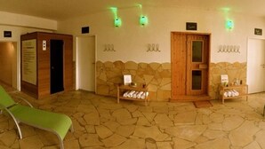 Um espaço de spa com piso de pedra, cadeiras de descanso verde, sauna de madeira e parede de pedra.