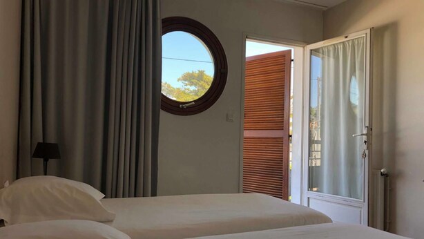 Quarto com duas camas, janela com vista para árvores e porta que dá para o exterior.