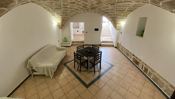 Uma sala de jantar com mesa e cadeiras, um sofá e uma escada que leva a um andar superior.