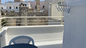 Terraço no telhado com mesa e cadeiras, vista para uma cidade histórica com ruínas antigas e edifícios modernos.