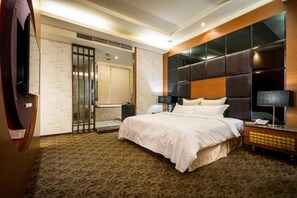 Quarto de hotel com uma cama grande, cabeceira de madeira, televisão de tela plana e mesa de cabeceira com abajur.