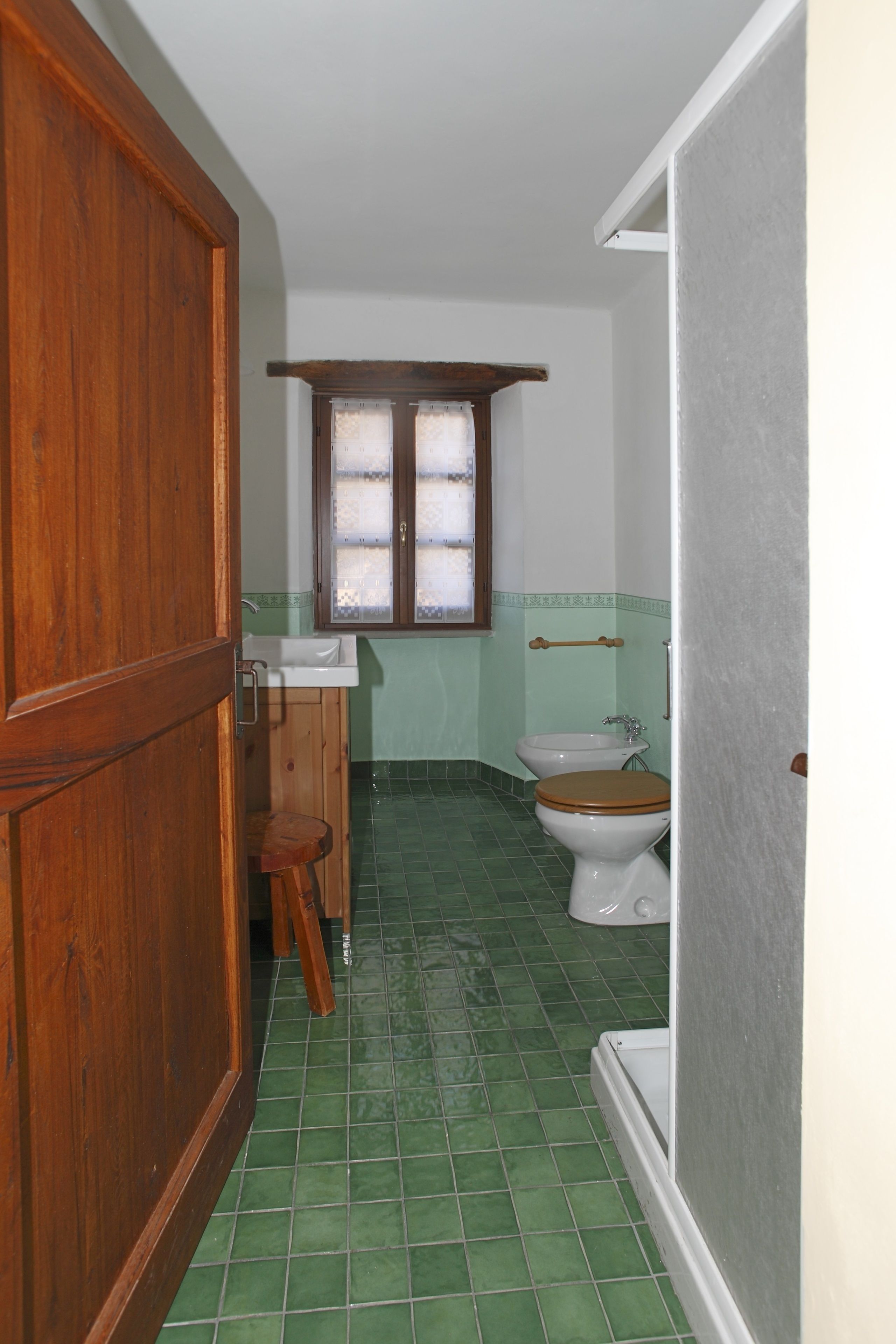 Um banheiro com porta de madeira, janela, pia, vaso sanitário e banheira.
