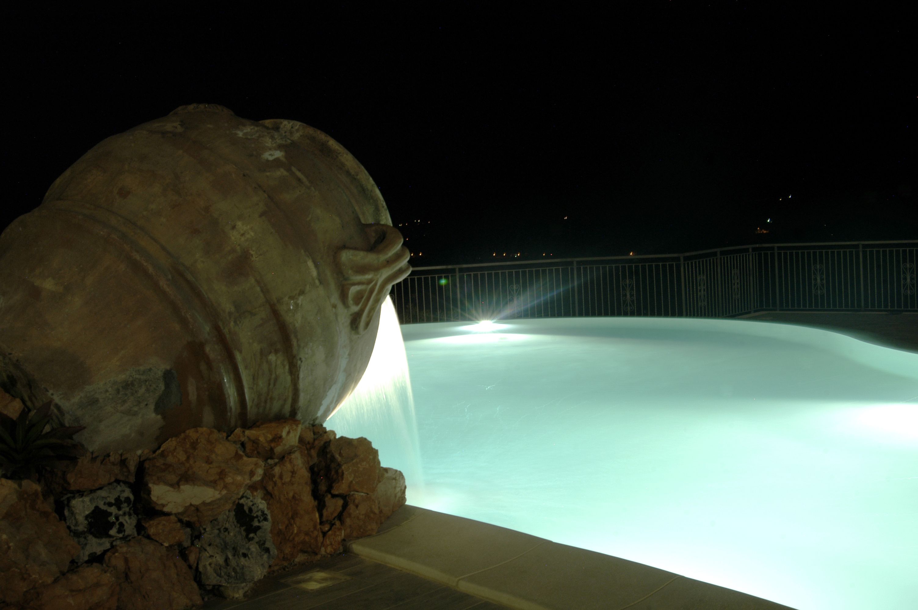 Escultura grande e iluminada em uma área de piscina à noite.