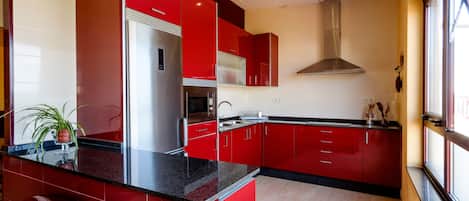 Cozinha moderna com armários vermelhos, eletrodomésticos de aço inoxidável e bancada preta.