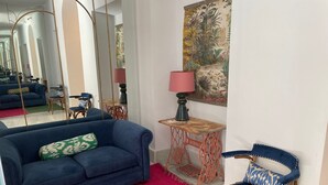 Uma sala de estar com um sofá azul, um tapete vermelho, uma cadeira de madeira e uma mesa com abajur.