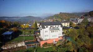 Zona residencial com um edifício branco imponente, com varanda, rodeada por vegetação exuberante e um cenário de colinas.