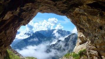 Entrada de caverna com vista para montanhas e nuvens.