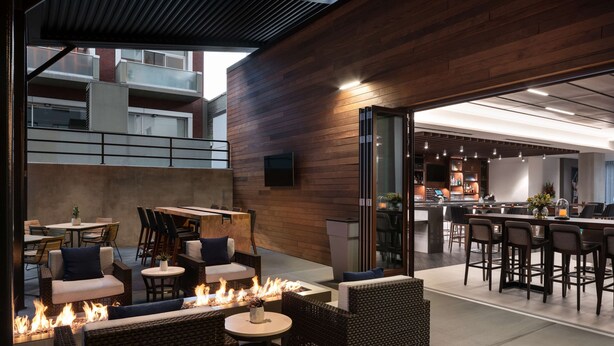 Área externa com mobiliário de vime e lareira, adjacente a um bar e espaço de refeições com decoração moderna.