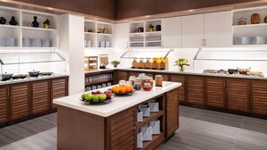 Cozinha moderna com armários de madeira, bancadas brancas e uma ilha central com frutas e potes.