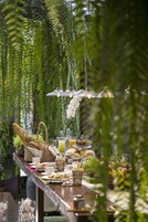 Um buffet de café da manhã com diversas opções de comidas e bebidas, com um cenário de plantas pendentes.