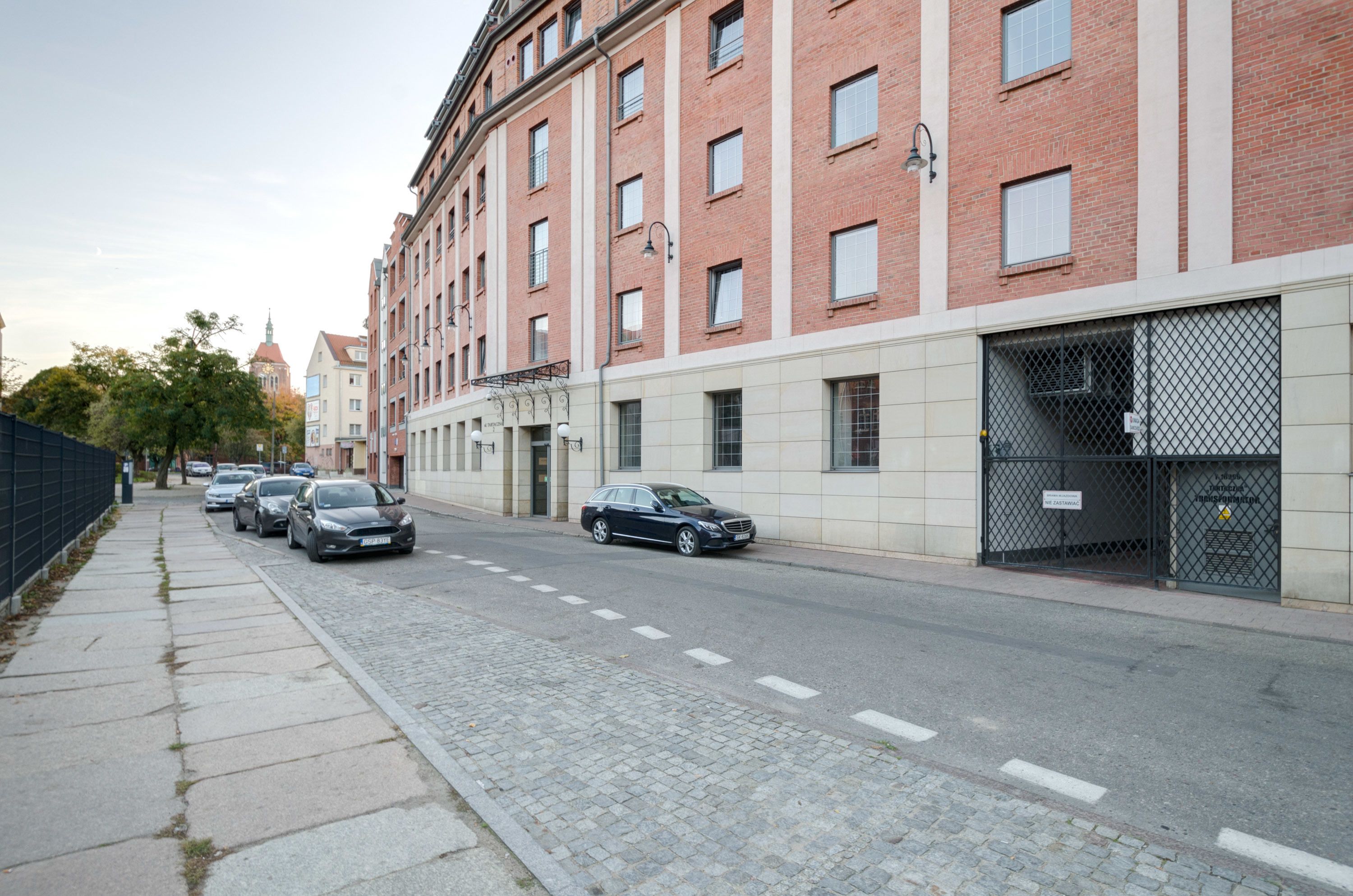Rua com carros estacionados e um edifício com várias janelas e portão.