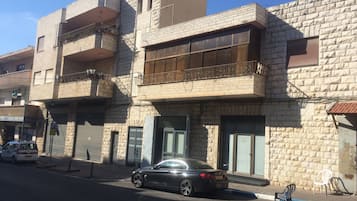 Um edifício com várias andares, fachada de pedra, varandas e um carro estacionado.