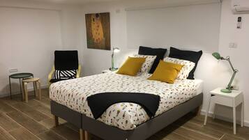 Quarto moderno com uma cama grande, uma cadeira, uma mesinha e um quadro na parede.