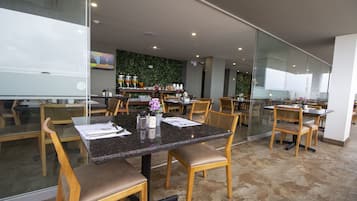 Uma área de refeições moderna com divisórias de vidro, cadeiras de madeira e uma mesa central com um menu.