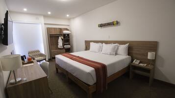 Quarto de hotel com uma cama grande, uma escrivaninha com luminária, um guarda-roupa e uma televisão fixada na parede.