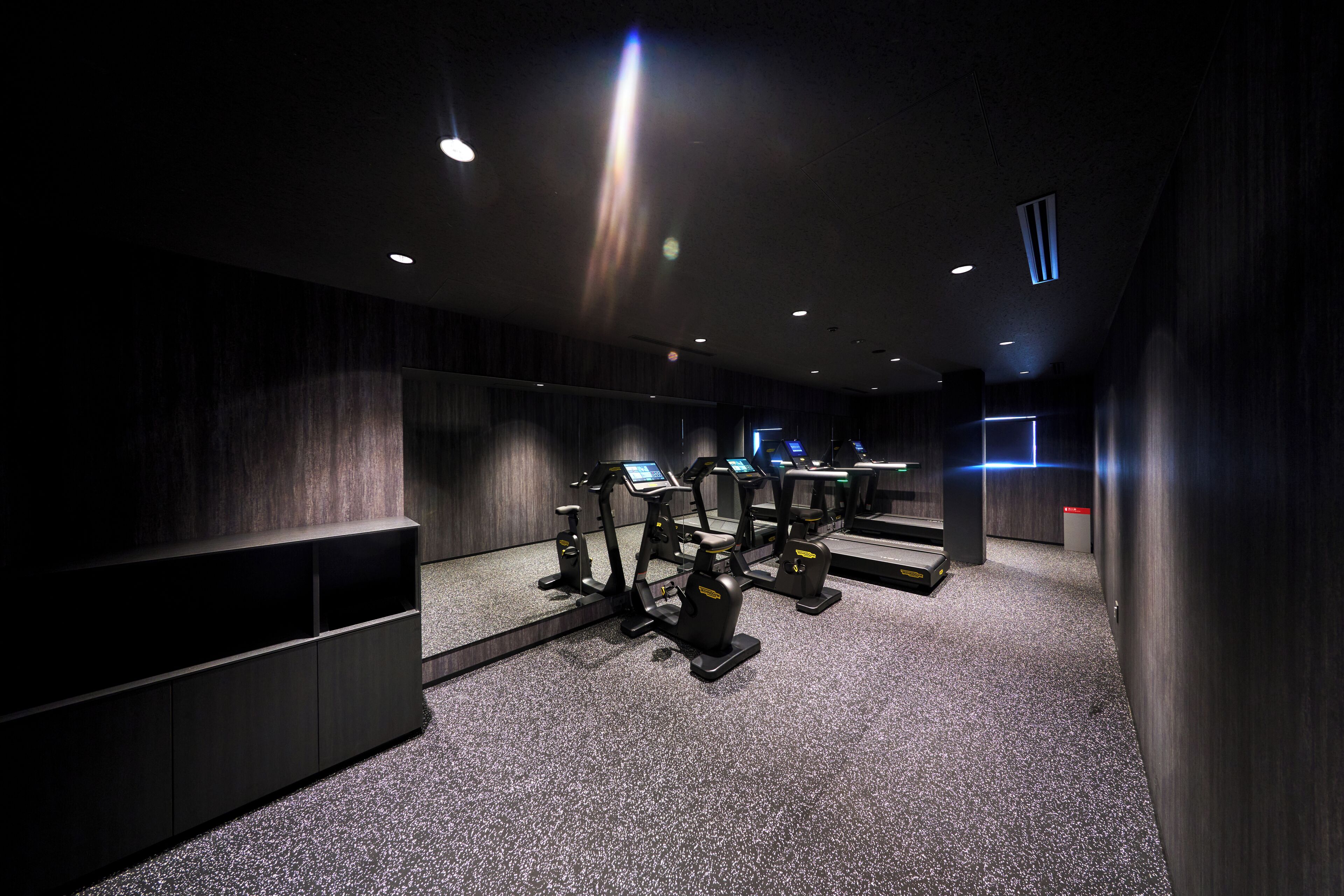 Academia moderna com várias esteiras e equipamentos de ginástica, iluminação fraca e interior escuro.