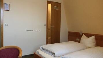 Quarto de hotel com duas camas, uma cabeceira de madeira, uma cadeira vermelha e uma porta com um aviso.