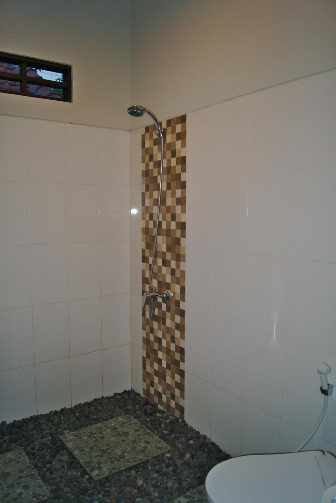 Um chuveiro com parede de azulejos xadrez, piso cerâmico e uma tomada elétrica visível.