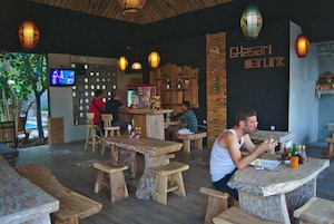 Interior de restaurante com mesas e bancos de madeira, uma tela de televisão e um quadro na parede.