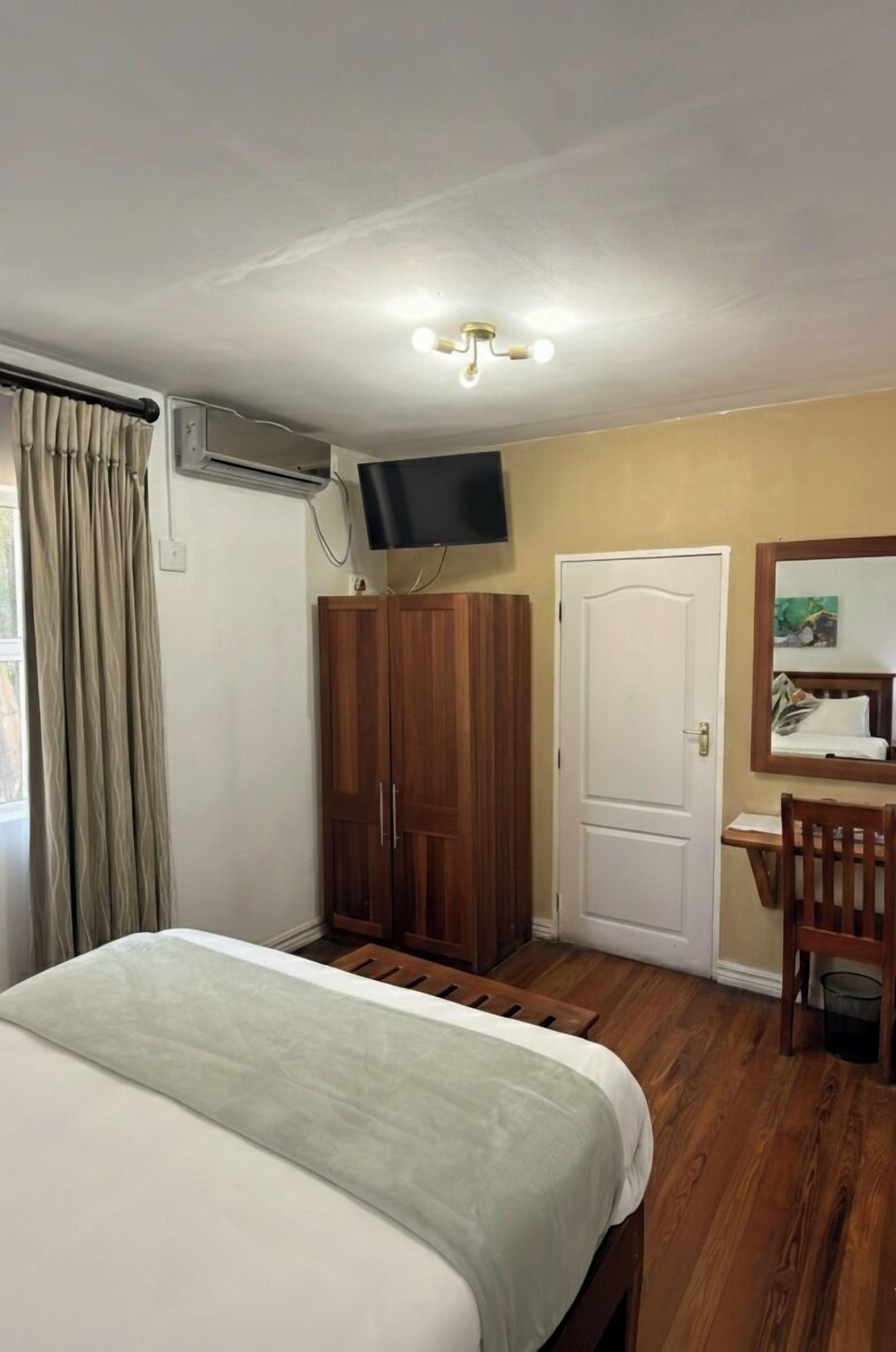Quarto de hotel com cama, guarda-roupa, escrivaninha com cadeira, televisão e porta.