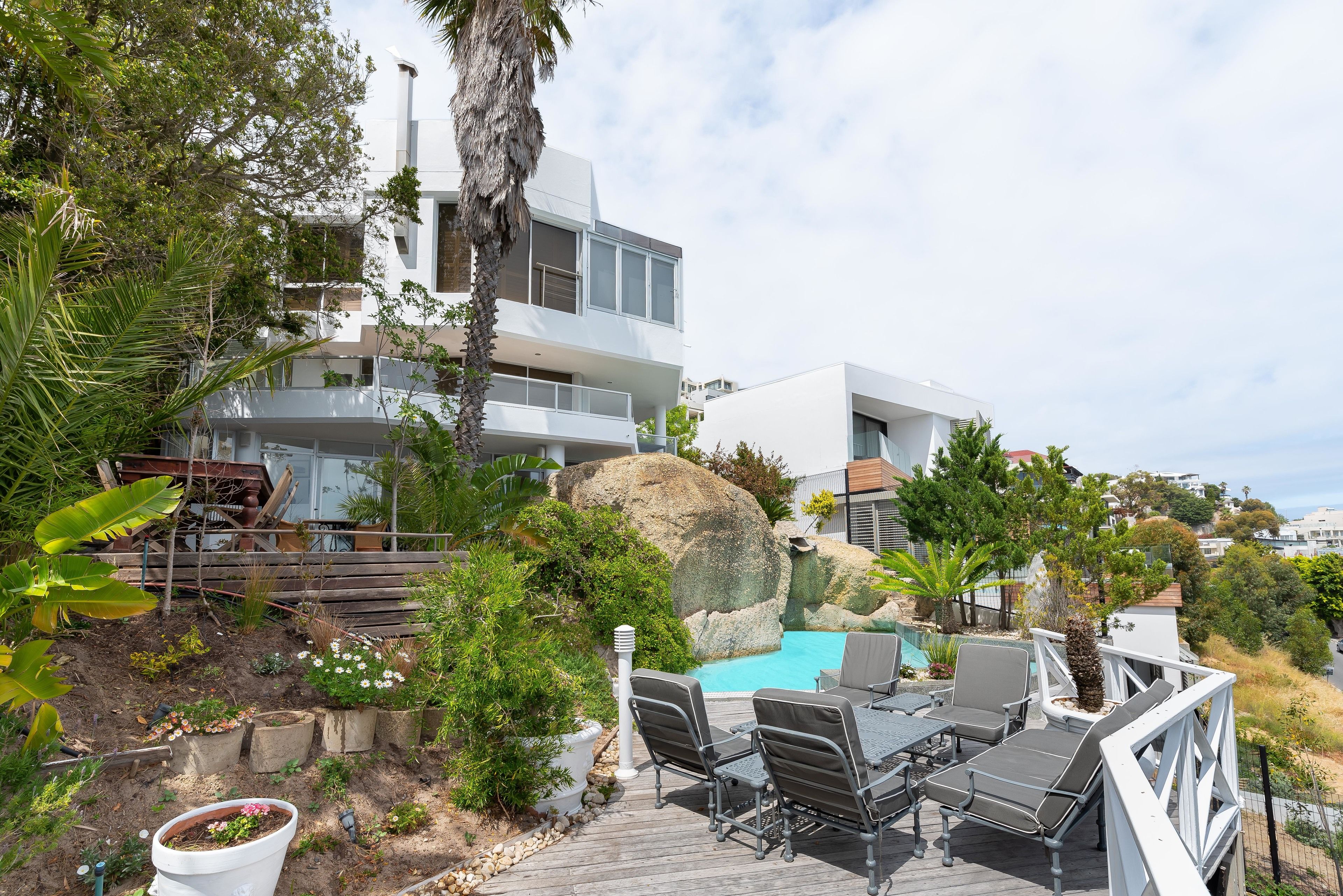 Um deck moderno ao ar livre com piscina, rodeado por vegetação exuberante e uma rocha grande.