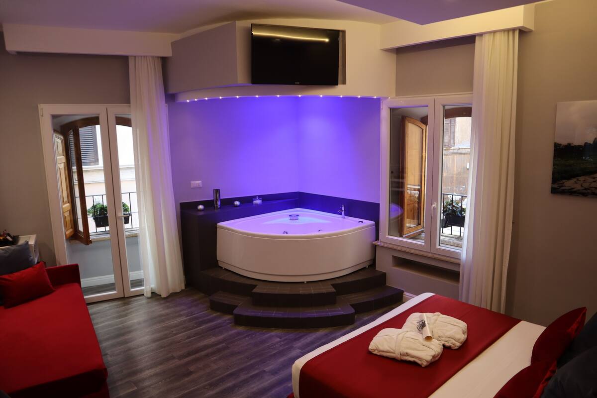 Quarto de hotel moderno com uma cama grande, uma banheira de hidromassagem integrada e uma TV fixada na parede.