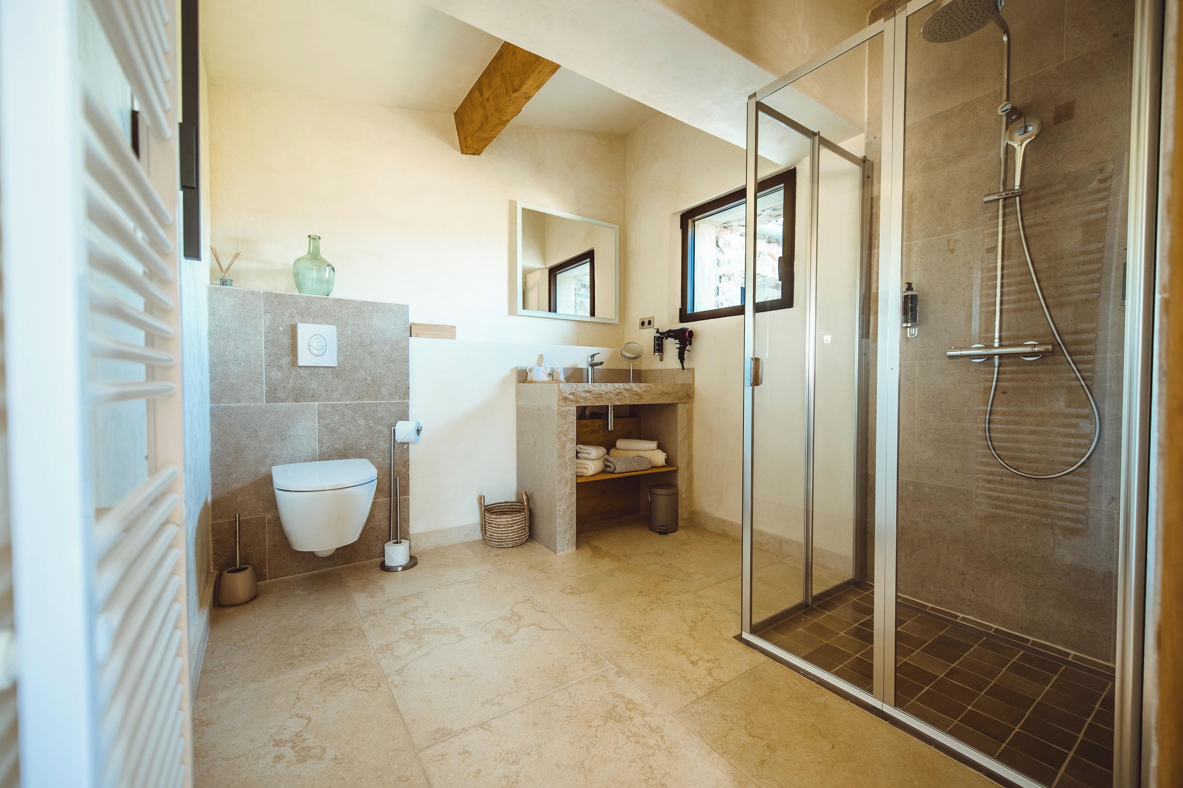 Uma casa de banho moderna com chuveiro de vidro, sanita, lavatório com espelho e porta-toalhas.