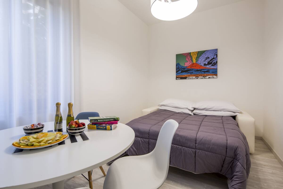 Quarto com cama, mesa branca com café da manhã e um quadro na parede.