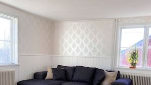 Quarto de canto com sofá seccional azul escuro, papel de parede estampado em branco e radiador perto da janela.
