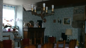 Uma sala de jantar com lustre, cadeiras de madeira, uma mesa com toalha de mesa florida e lareira de pedra.