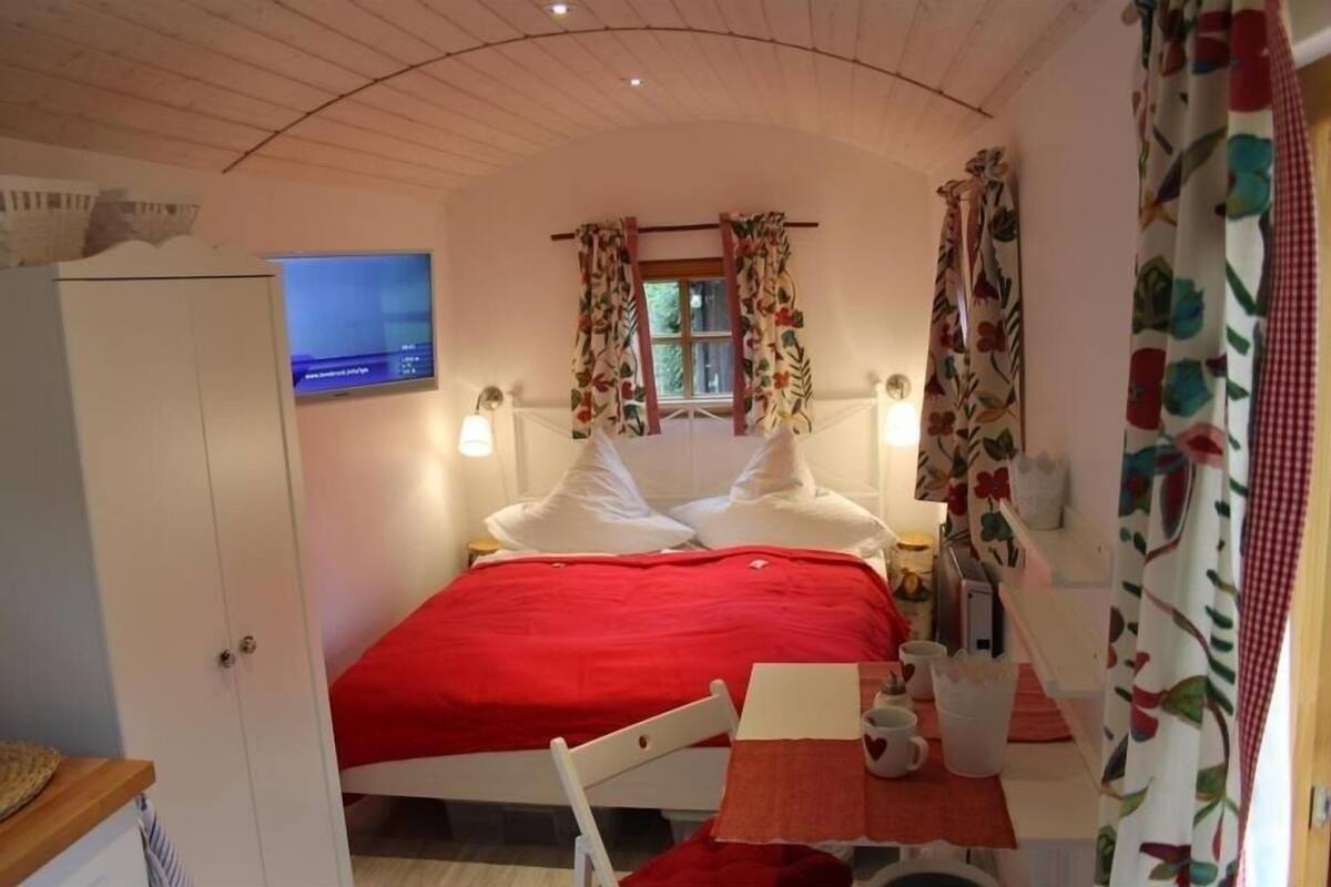Quarto com cama, televisão, escrivaninha e janela com cortinas.