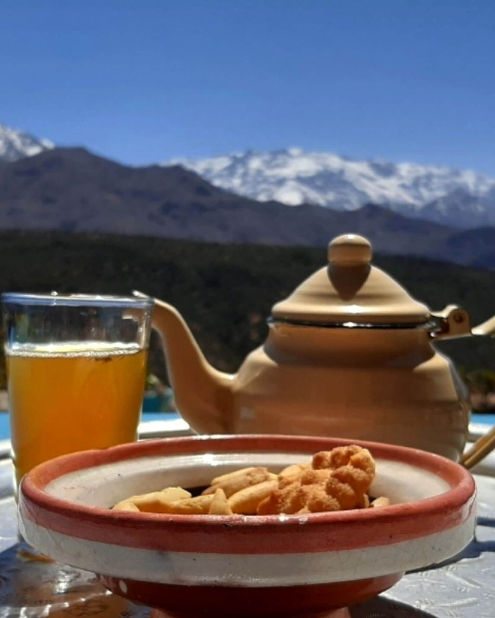 Uma mesa posta com um bule, uma xícara de chá e uma tigela de comida, com vista para as montanhas ao fundo.