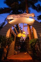 Entrada para o Agonda Serenity Resort & Restaurant, com uma placa acima do arco, cercada por palmeiras e um caminho que leva para o interior.