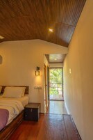 Quarto com teto de madeira, uma cama, mesa de cabeceira e luminária fixada na parede.