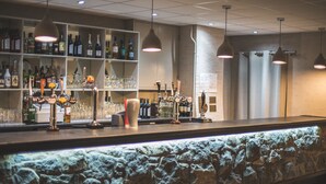 Uma área de bar com balcão de pedra, várias torneiras de cerveja, prateleiras com garrafas e iluminação pendente.