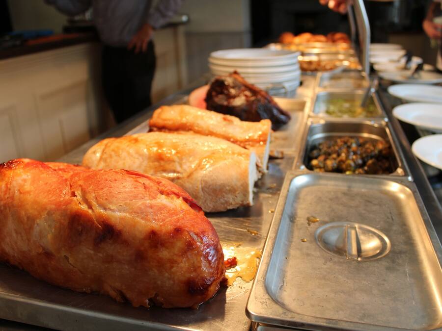 Buffet com diversos pratos, incluindo um assado grande, possivelmente um peru, e outras opções em bandejas de metal.