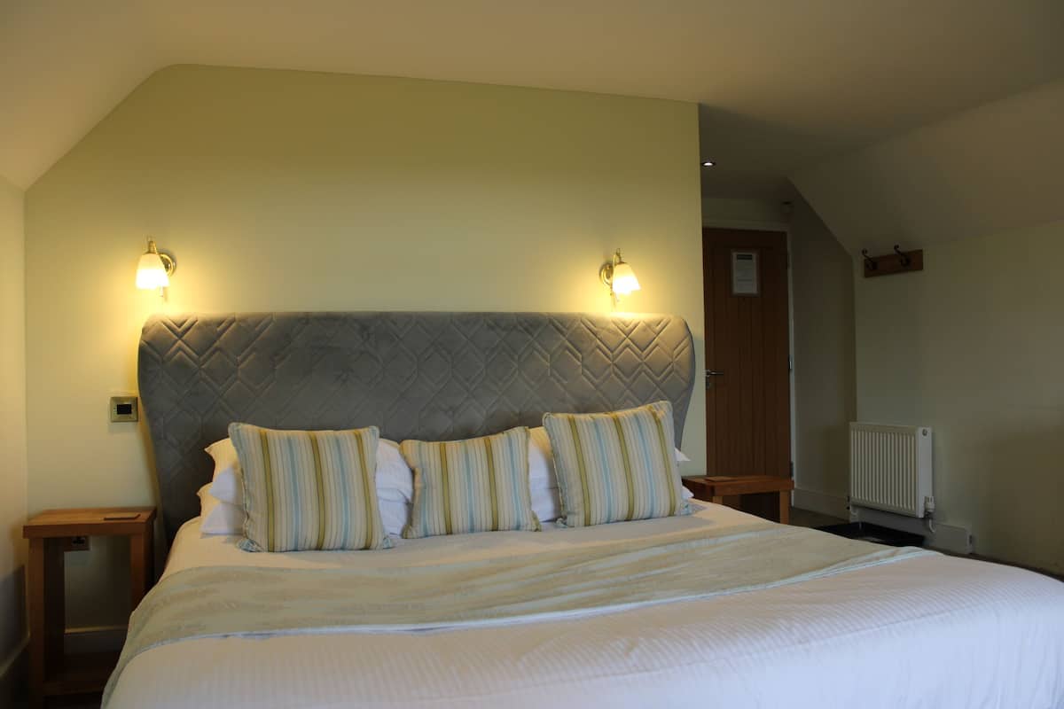 Quarto de hotel com uma cama grande, duas mesas de cabeceira, uma cabeceira e duas luminárias fixadas na parede.