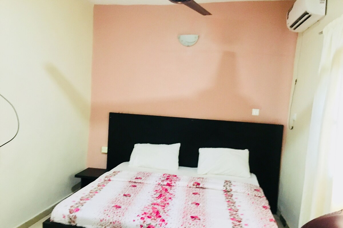 Uma cama de solteiro com cabeceira preta em quarto com parede em tom de pêssego.