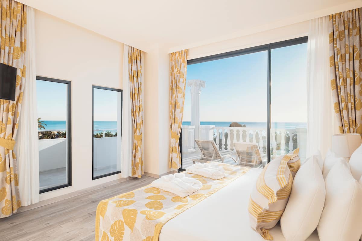 Quarto de hotel com uma cama grande, varanda com vista para o mar e televisão na parede.