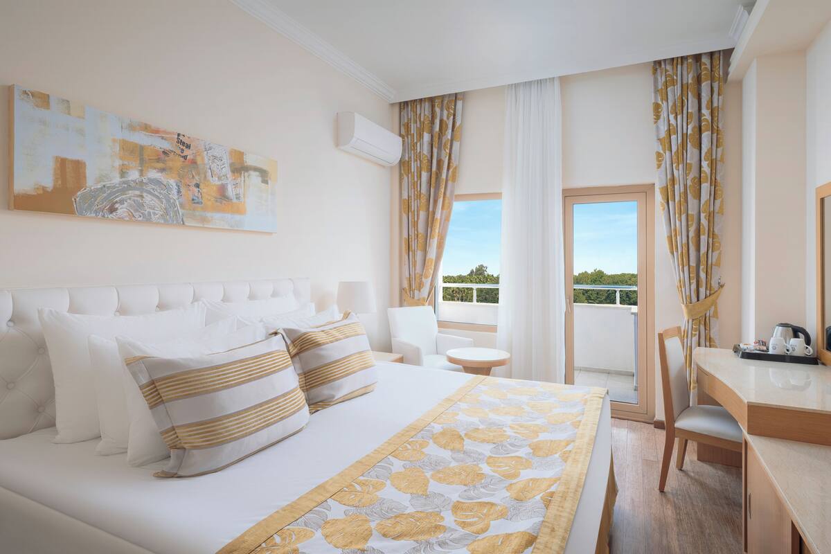 Quarto de hotel com cama, escrivaninha, cadeira e varanda com cortinas.