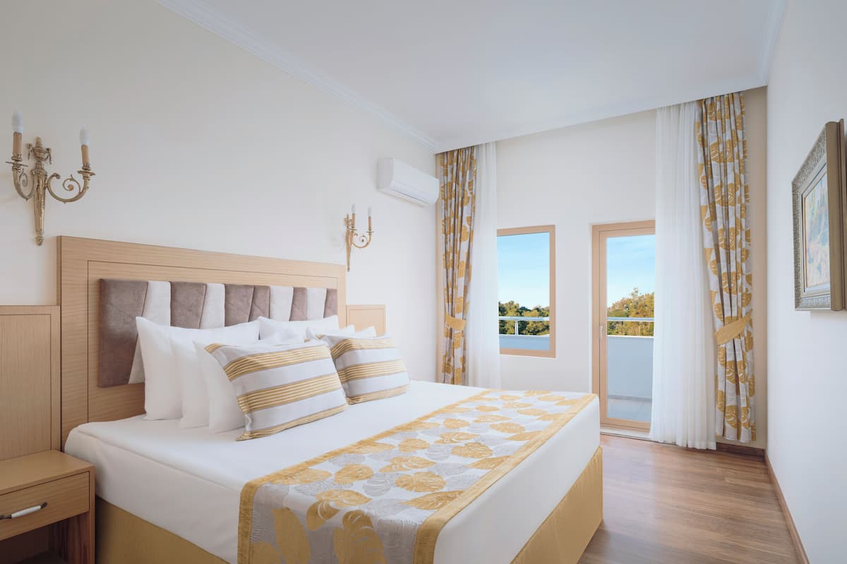 Quarto com uma cama grande, mesa de cabeceira, ar condicionado fixado na parede e vista para o exterior pela janela.