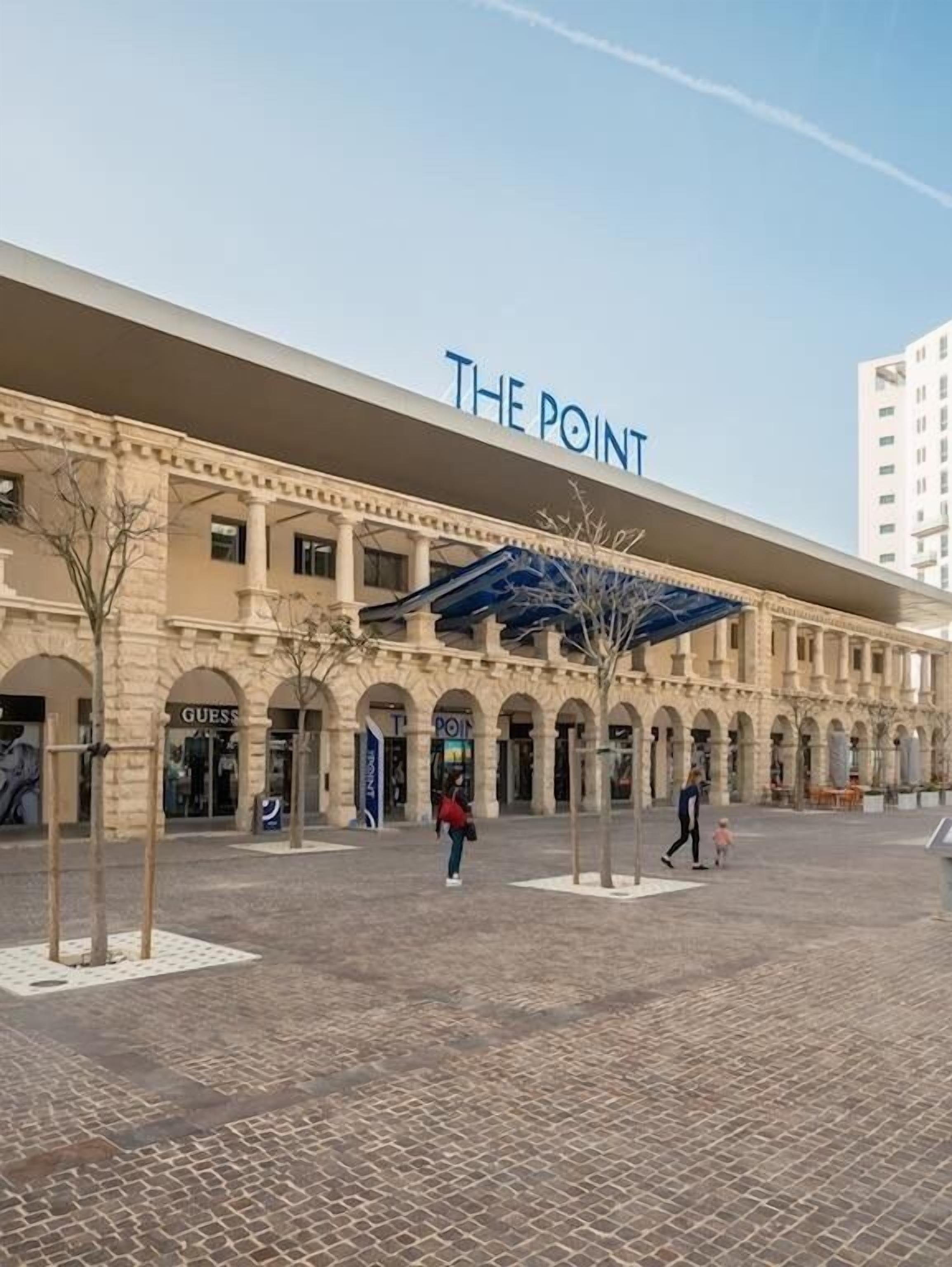 Um edifício com a sinalização "THE POINT", apresentando um estilo arquitetônico clássico com arcos e uma galeria coberta.