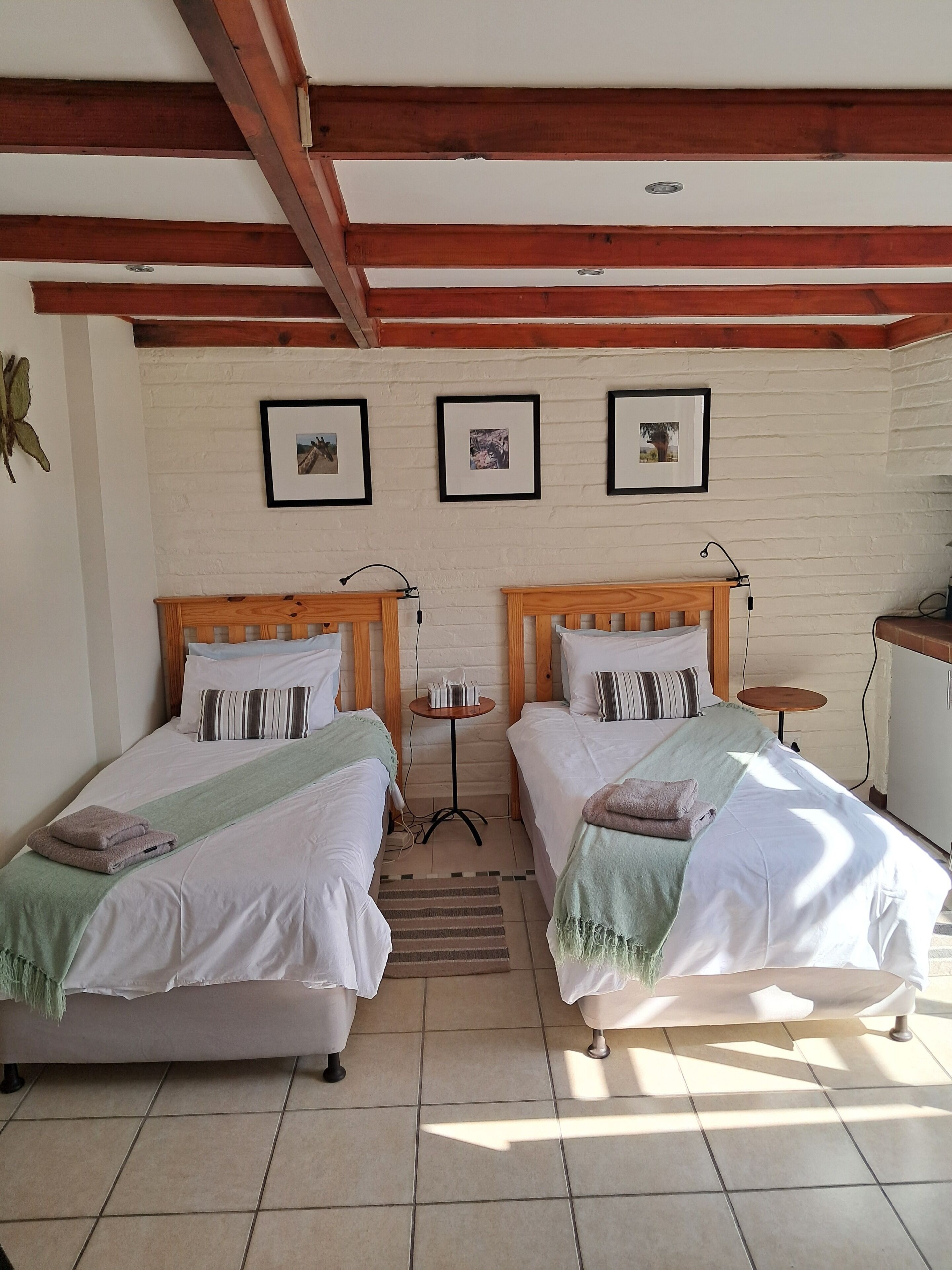 Quarto com duas camas, uma mesinha e um painel com três quadros.